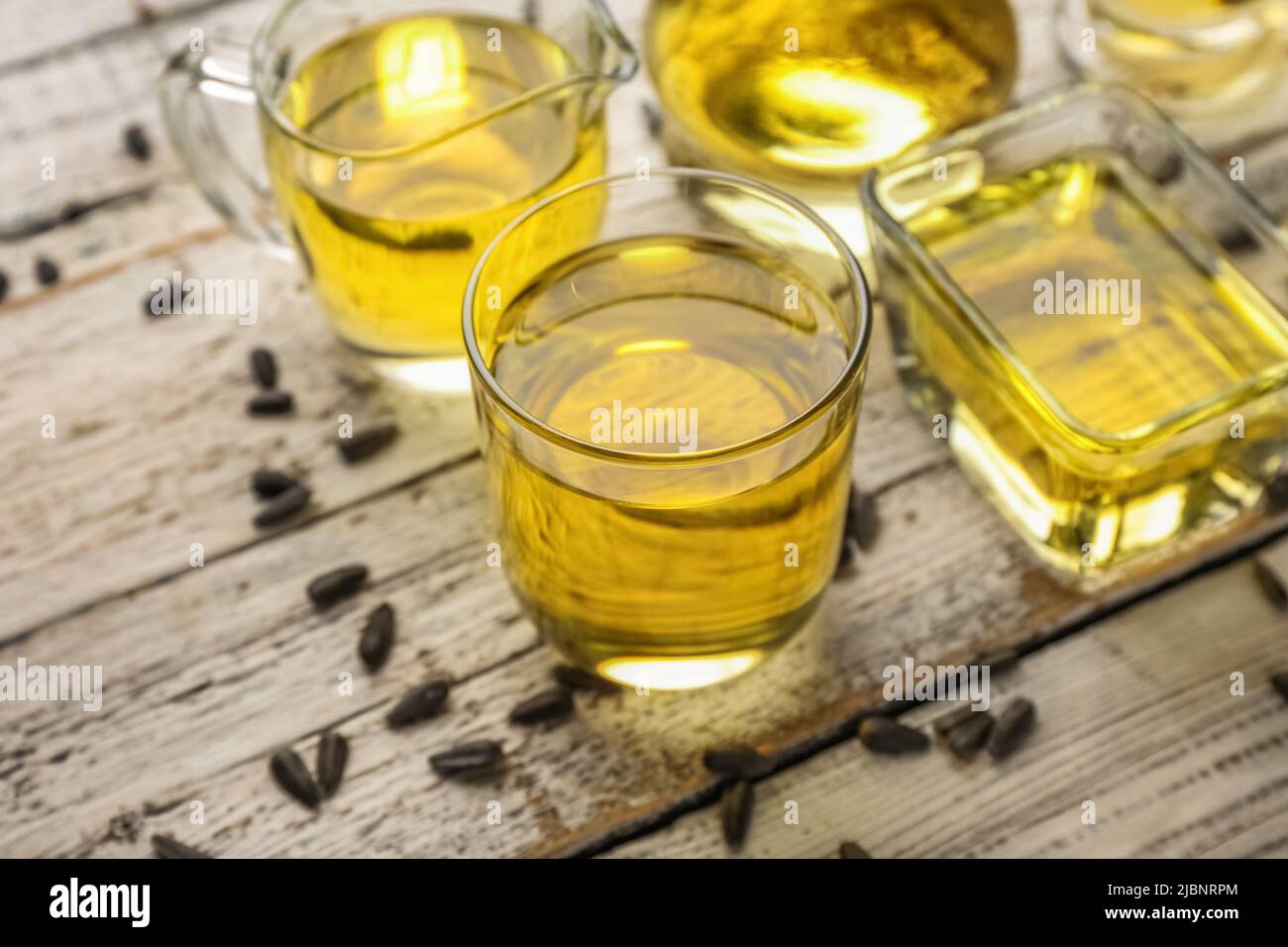 Glass containers and sunflower seeds on white wooden background ...