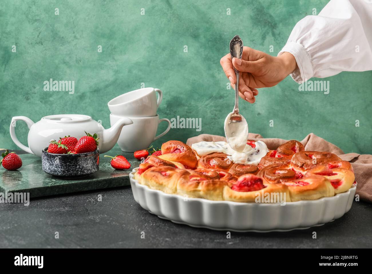 Female chef adding cream onto strawberry cinnamon rolls on table ...