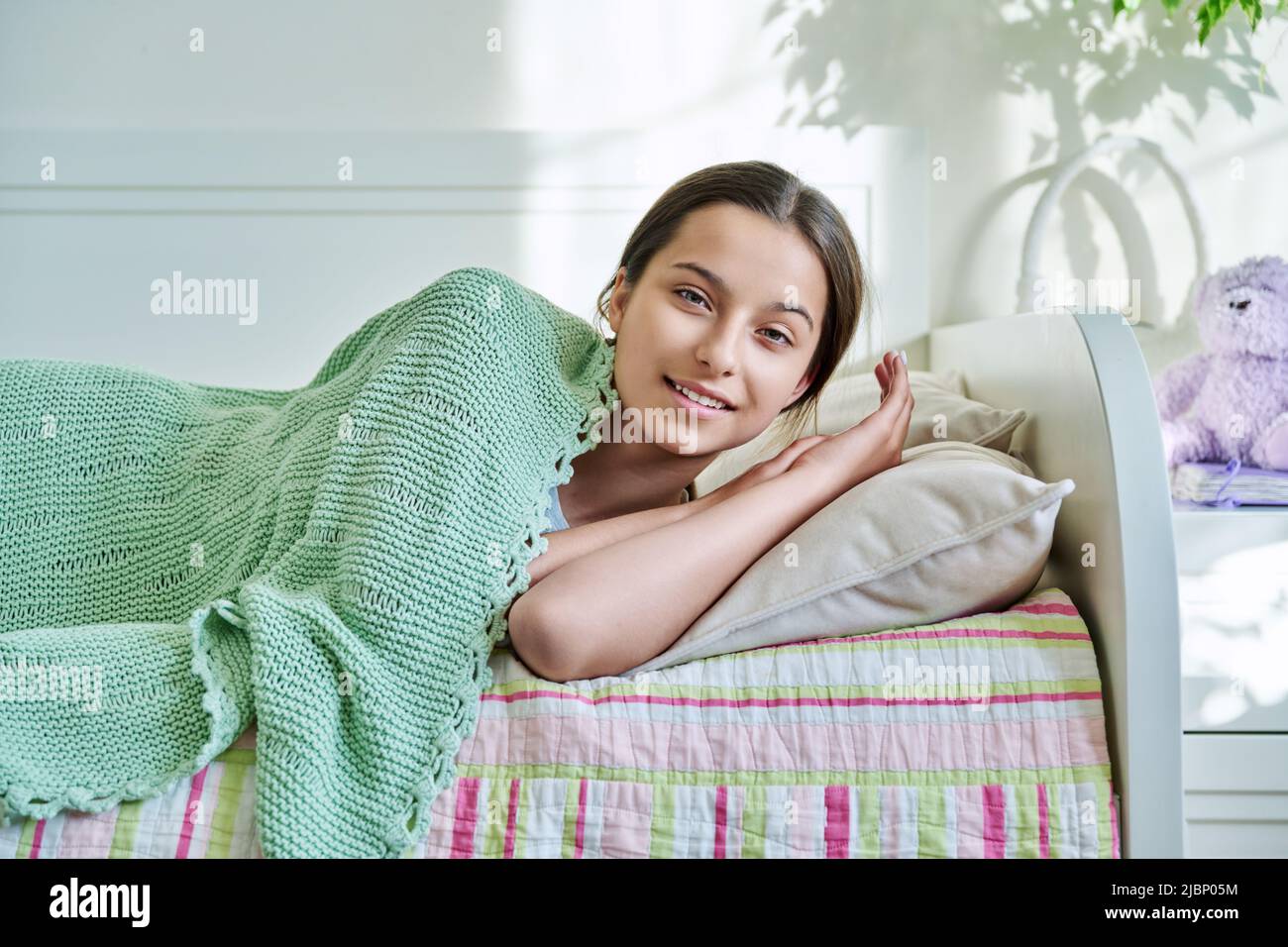 Teenage girl sleeping at home in bed, calm teenager looking at camera ...