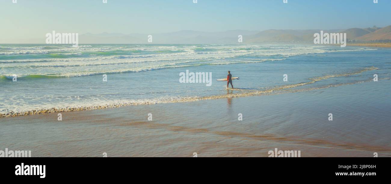 Seascape and silhouette of surfer with surf board, hills, and blue sky ...