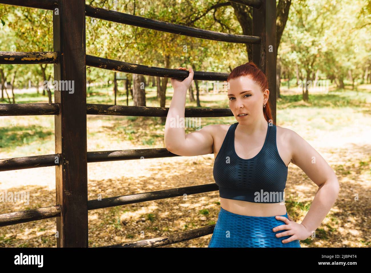 portrait of a young female athlete leaning on a public trellis outside ...