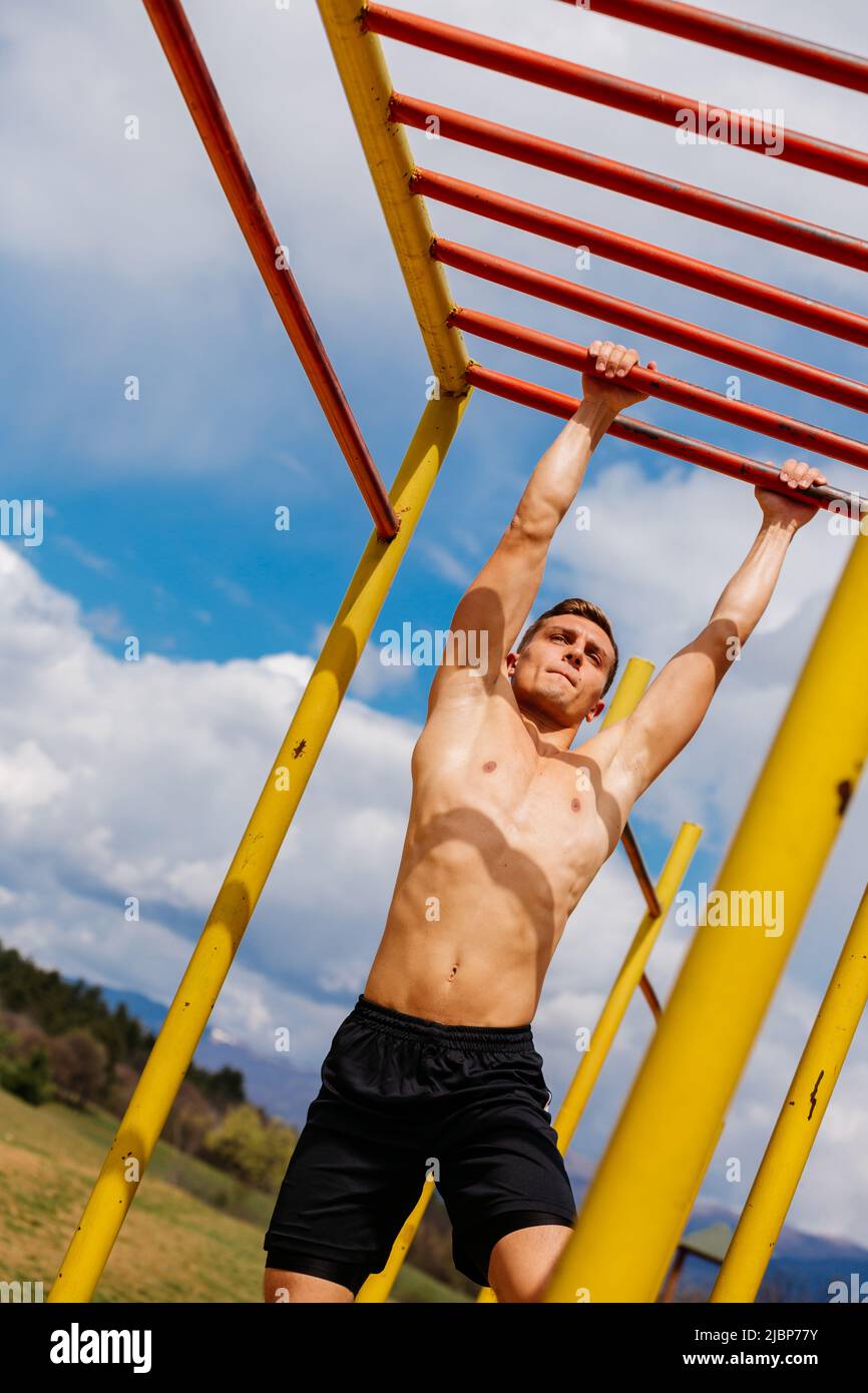 Athletic young man hanging from the bars at the calisthenics gym ...