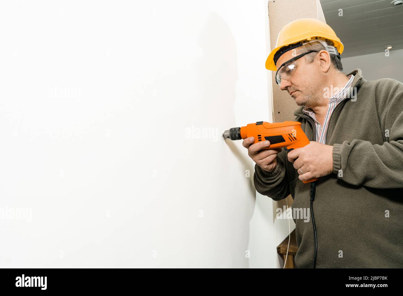 Construction Worker drilling a hole with a drill on a white wall. Copy ...