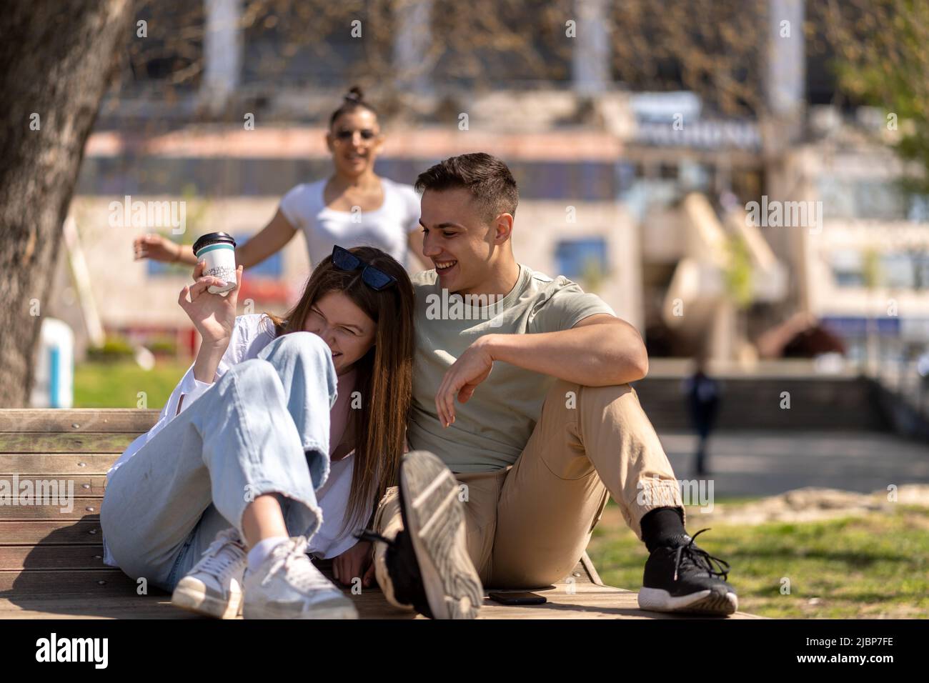 Friends or couple laughing and taking a conversation sitting on a bench ...
