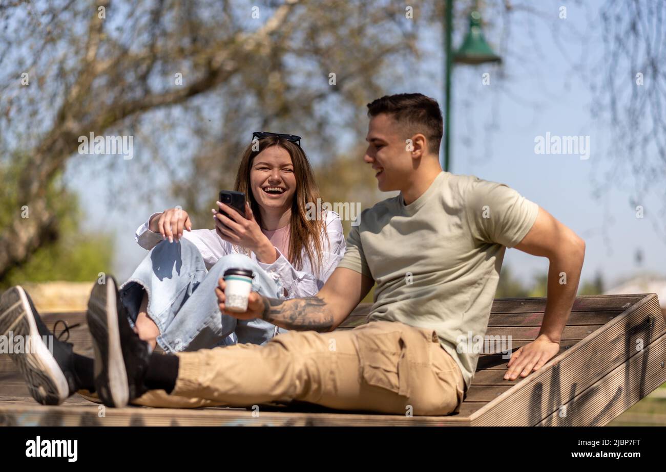 Portrait of a happy couple holding mobile phone while sitting on the ...