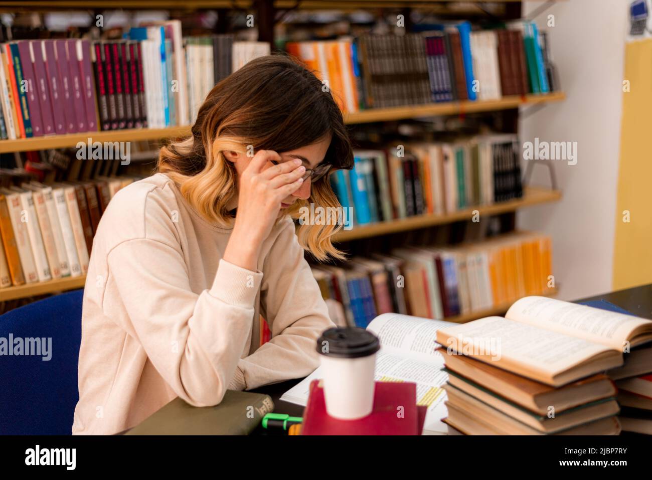 Beautiful girl studying on a desk in a library while adjusting her ...