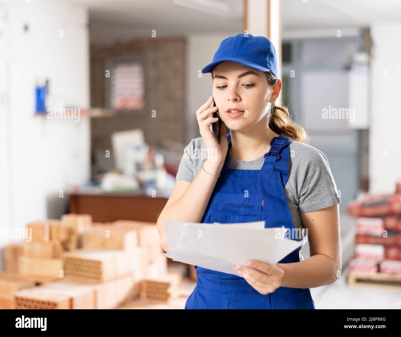 Female foreman holding papers and talking on phone at construction site ...