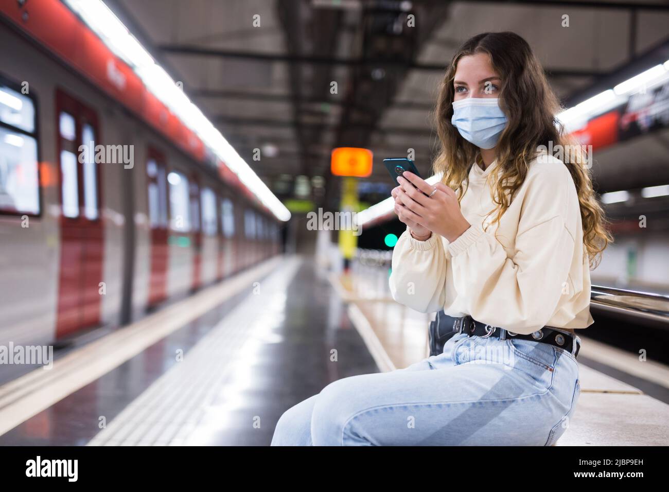 Girl in a protective mask sitting on a bench in the subway with a ...