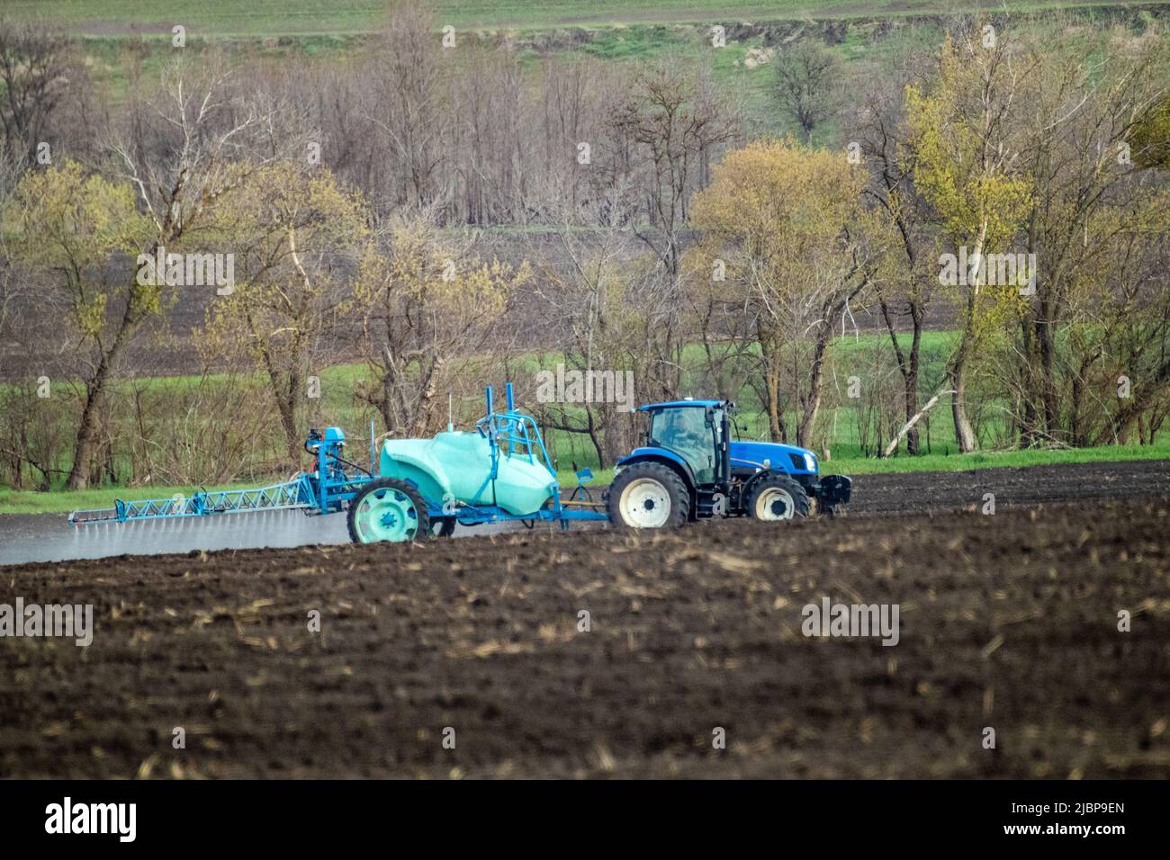 Blue tractor spraying insecticide on cultivated land field ...