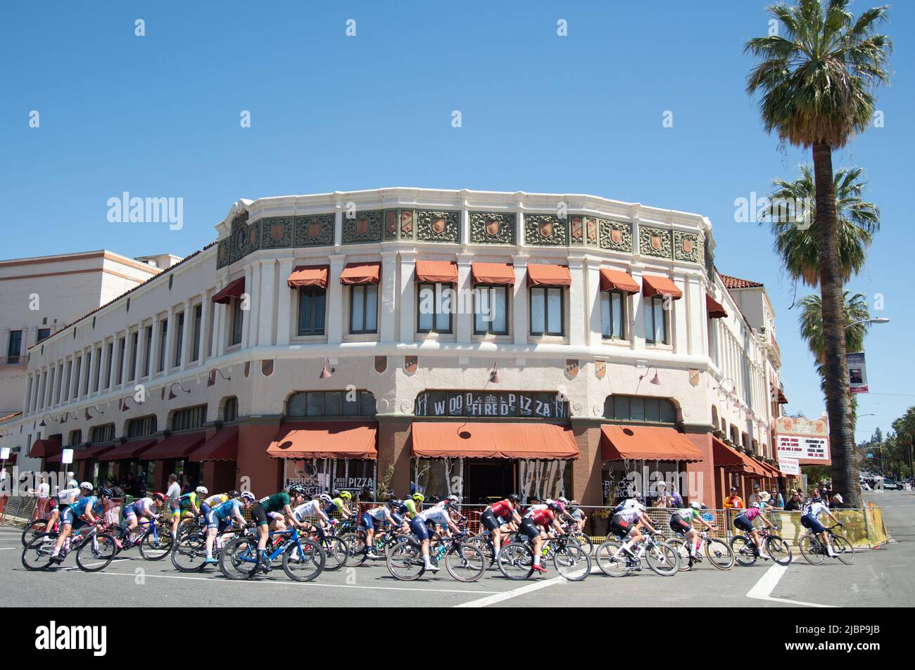 The men's peloton rounds a corner in historic Downtown Redlands, CA ...