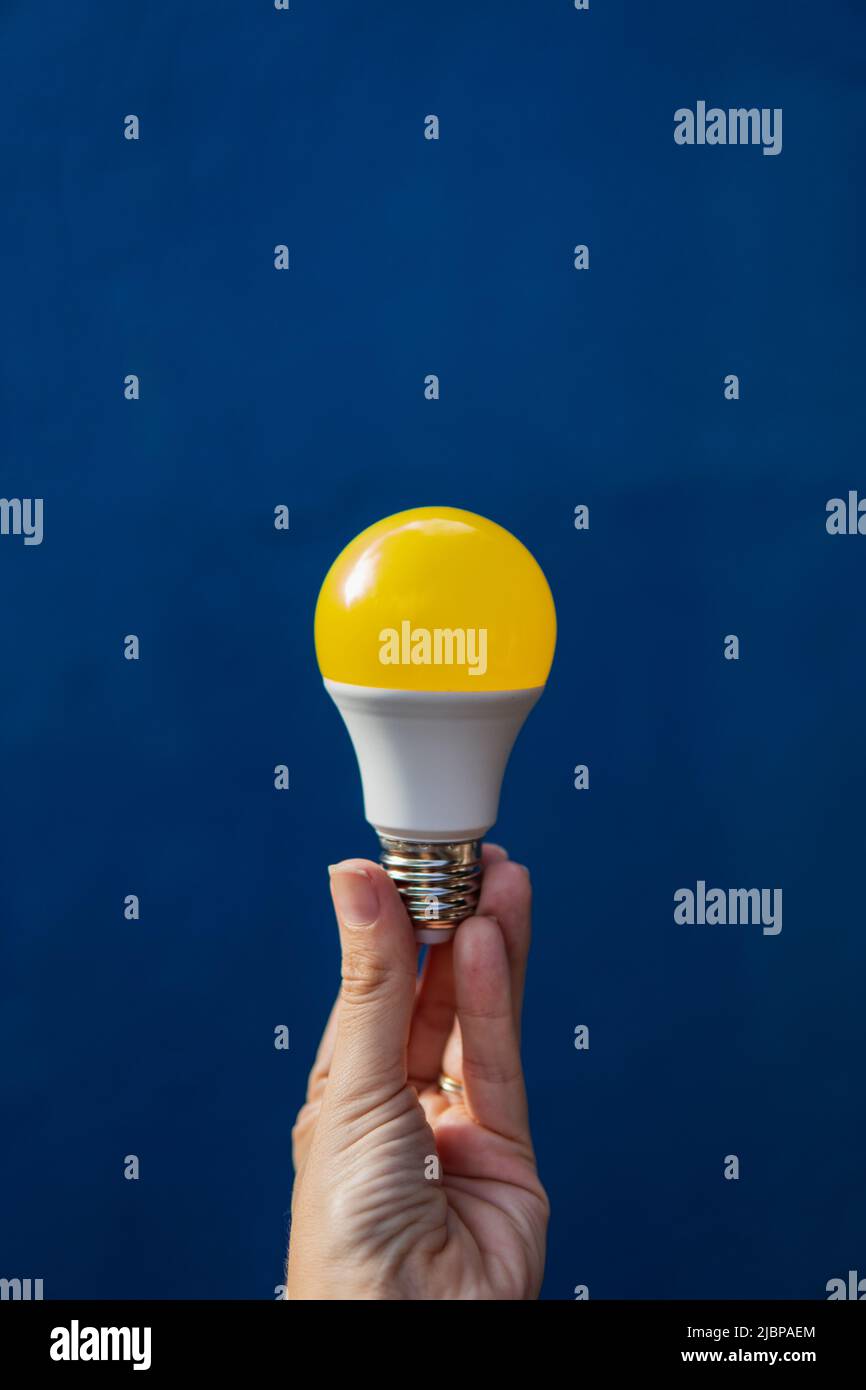 White hand holding yellow light bulb over a blue wall outdoor Stock ...