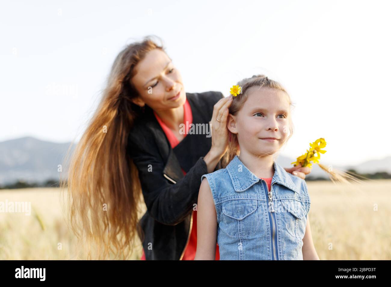 Mother braiding daughter's hair with yellow flowers in field Stock Photo - Alamy