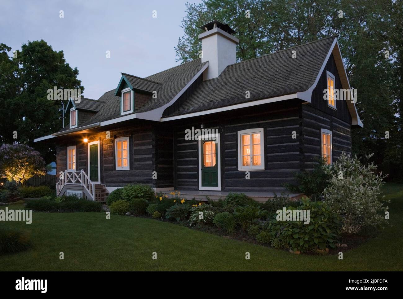 Old reconstructed 1800s log home with landscaped front yard at dusk ...