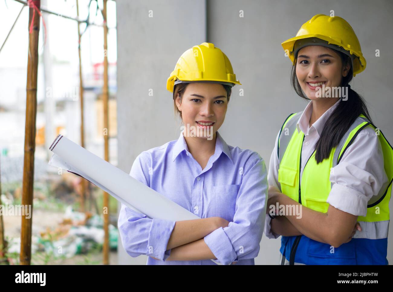 Young woman in construction helmet and floor plan stand with arms ...