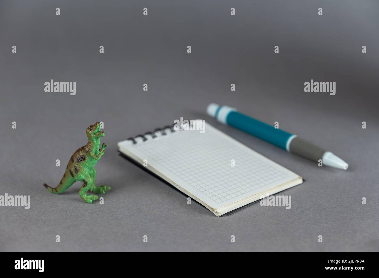 Dinosaur miniature, notepad and ballpoint pen against a gray background ...