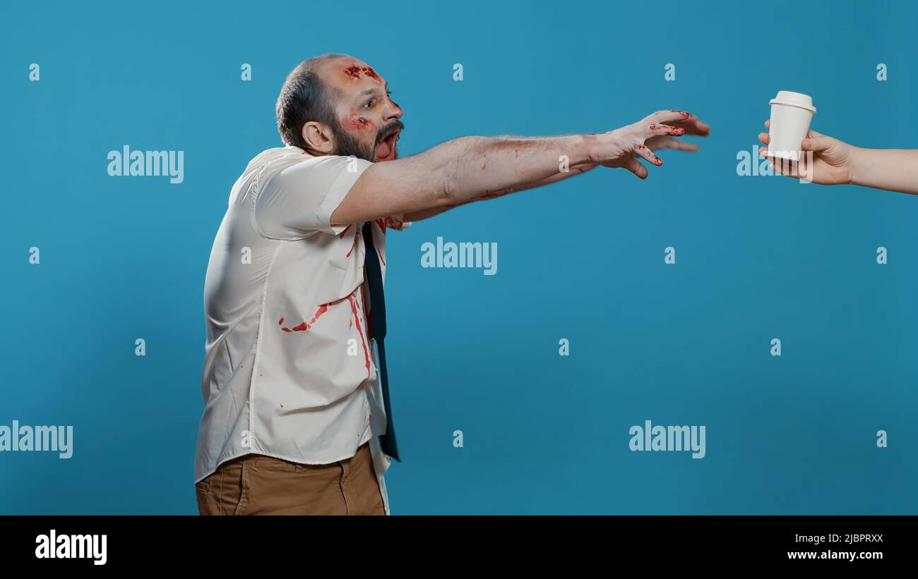 Angry ugly zombie trying to get cup of coffee on blue background ...