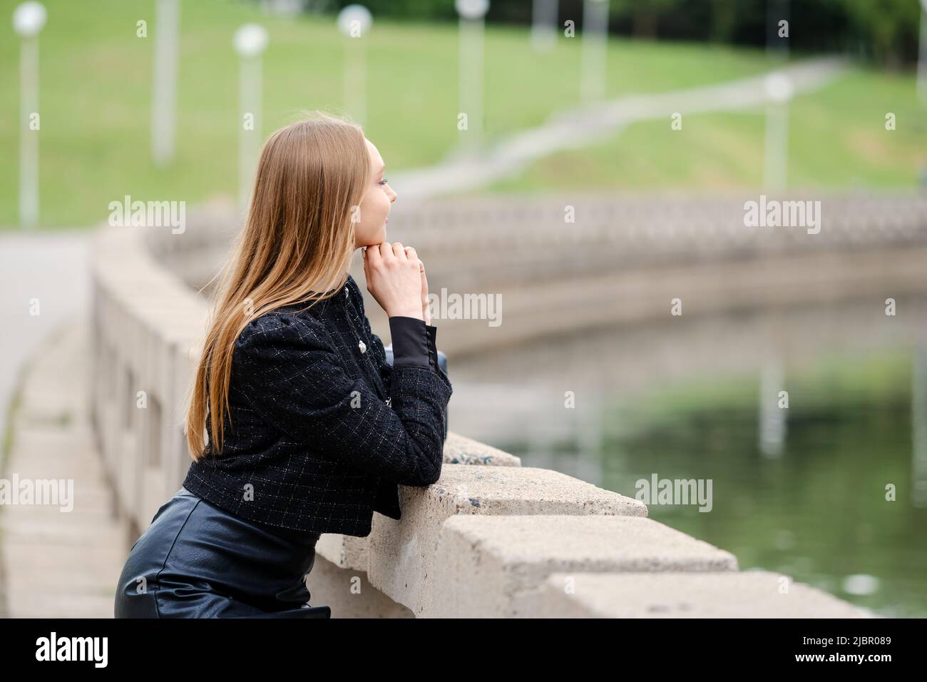 Young woman leans against the railing and looks thoughtfully at the ...