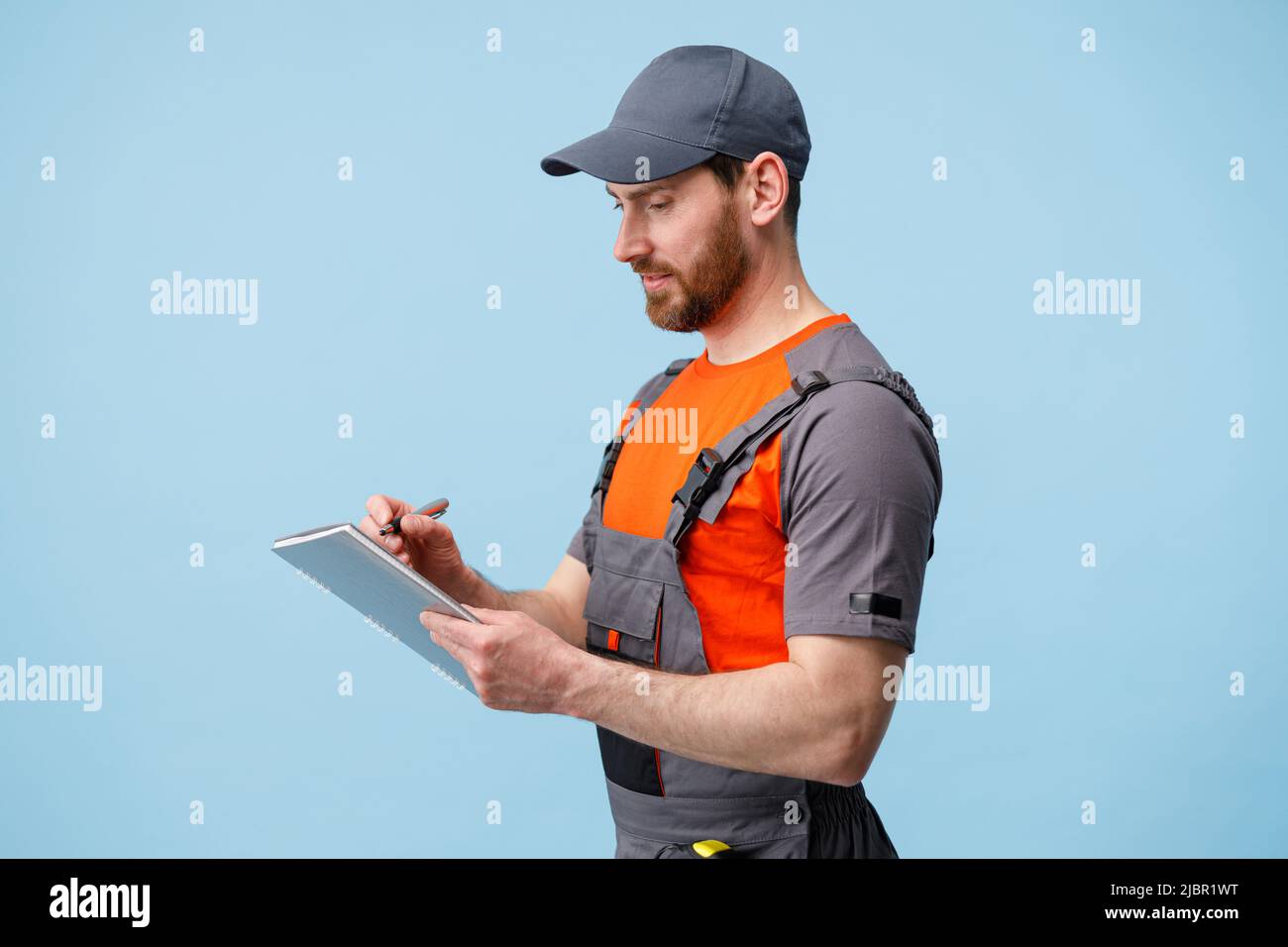 Focused Delivery man in uniform holding tablet and taking work notes ...