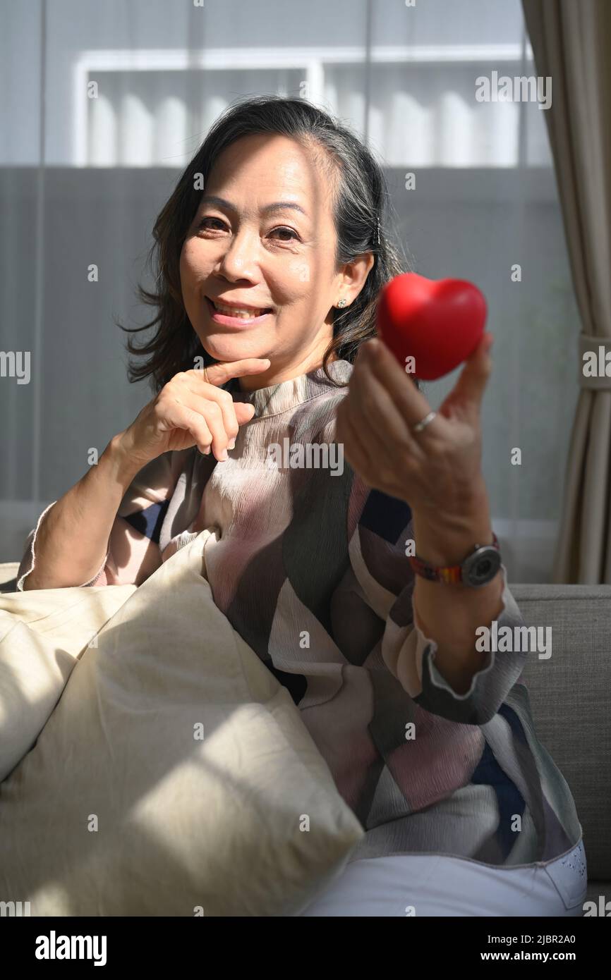 Middle aged woman holding heart shape and smiling at camera. Elderly ...