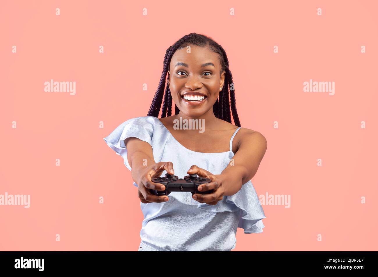 Excited millennial black lady with joystick playing video game on pink ...