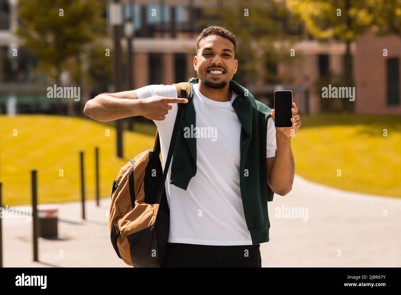 Great offer. Happy black guy standing outdoors, holding cellphone and ...