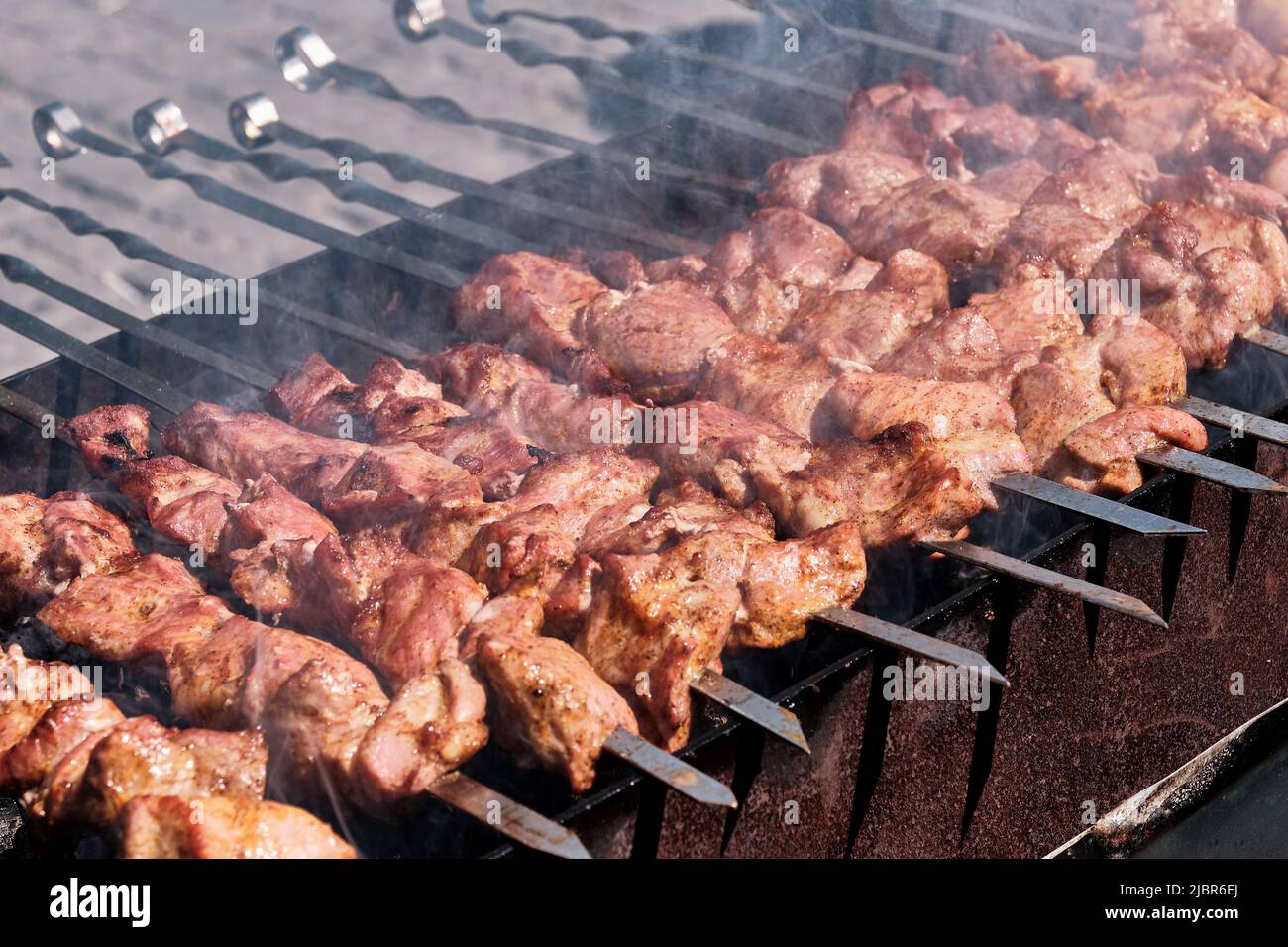 Pork kebab cooking on skewers on open fire at barbecue grill in park ...
