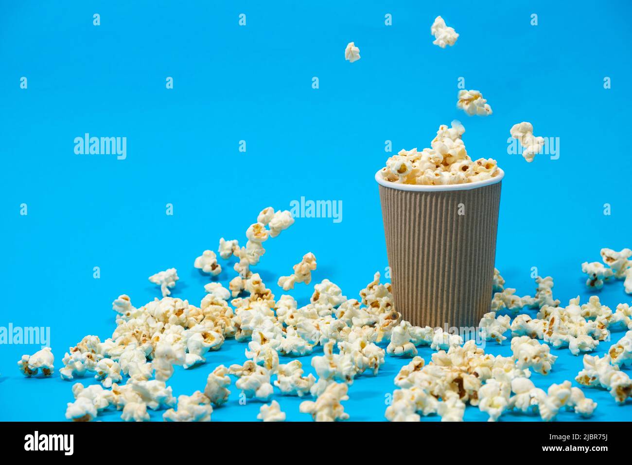 Popcorn is poured into a paper brown glass on a blue background with ...
