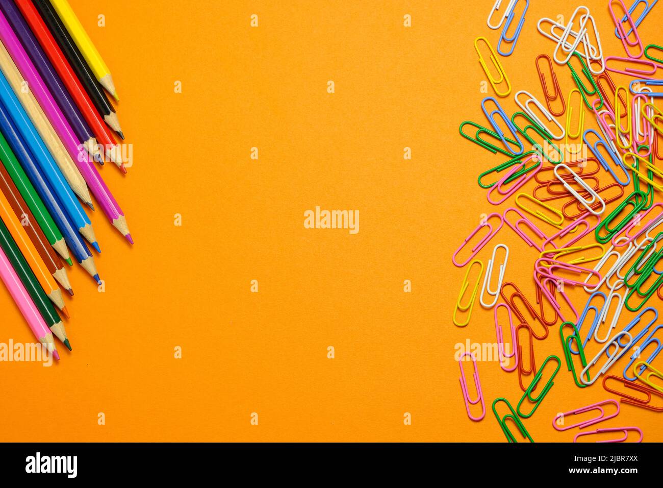 Colored pencils and stationery multi-colored paper clips on a orange ...