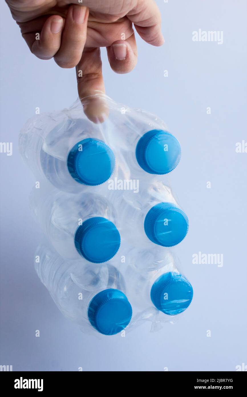 Six small plastic bottles of natural spring water hanging at finger on ...