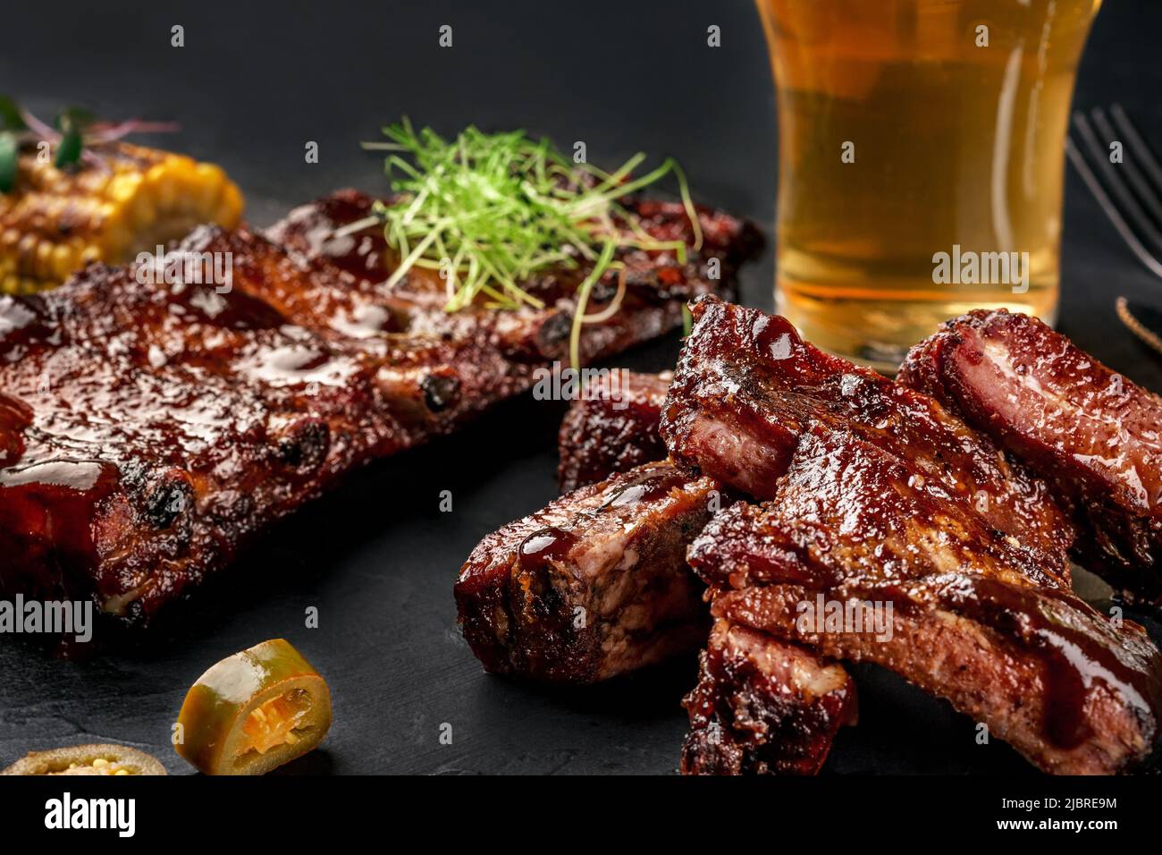 Pork ribs in barbecue sauce and a glass of beer on a black slate dish ...