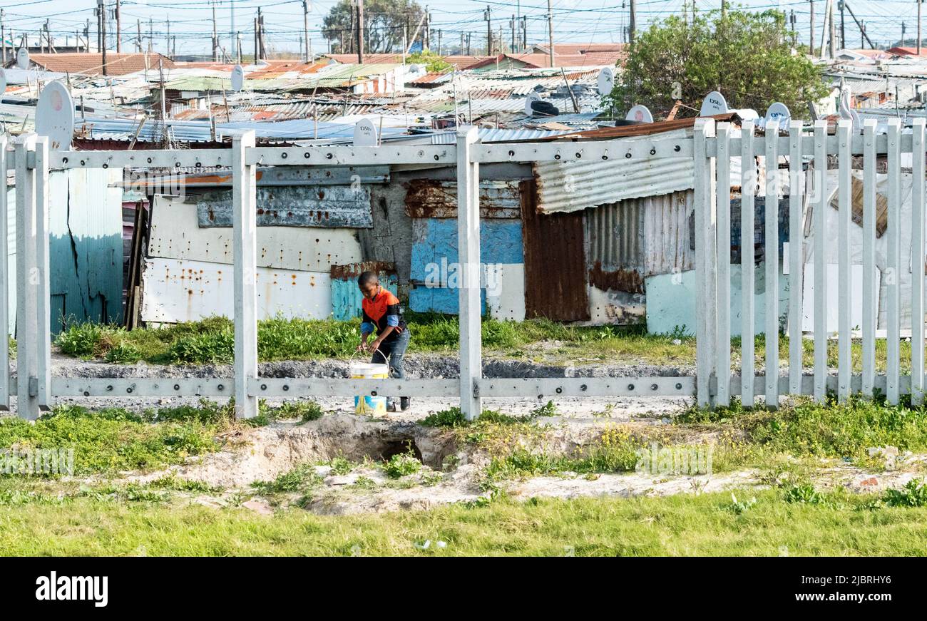 young black African boy carries a bucket in a township against a ...