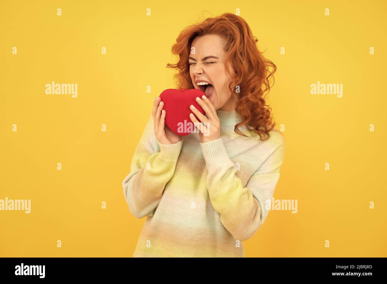 hungry redhead woman biting red heart on yellow background. love Stock ...