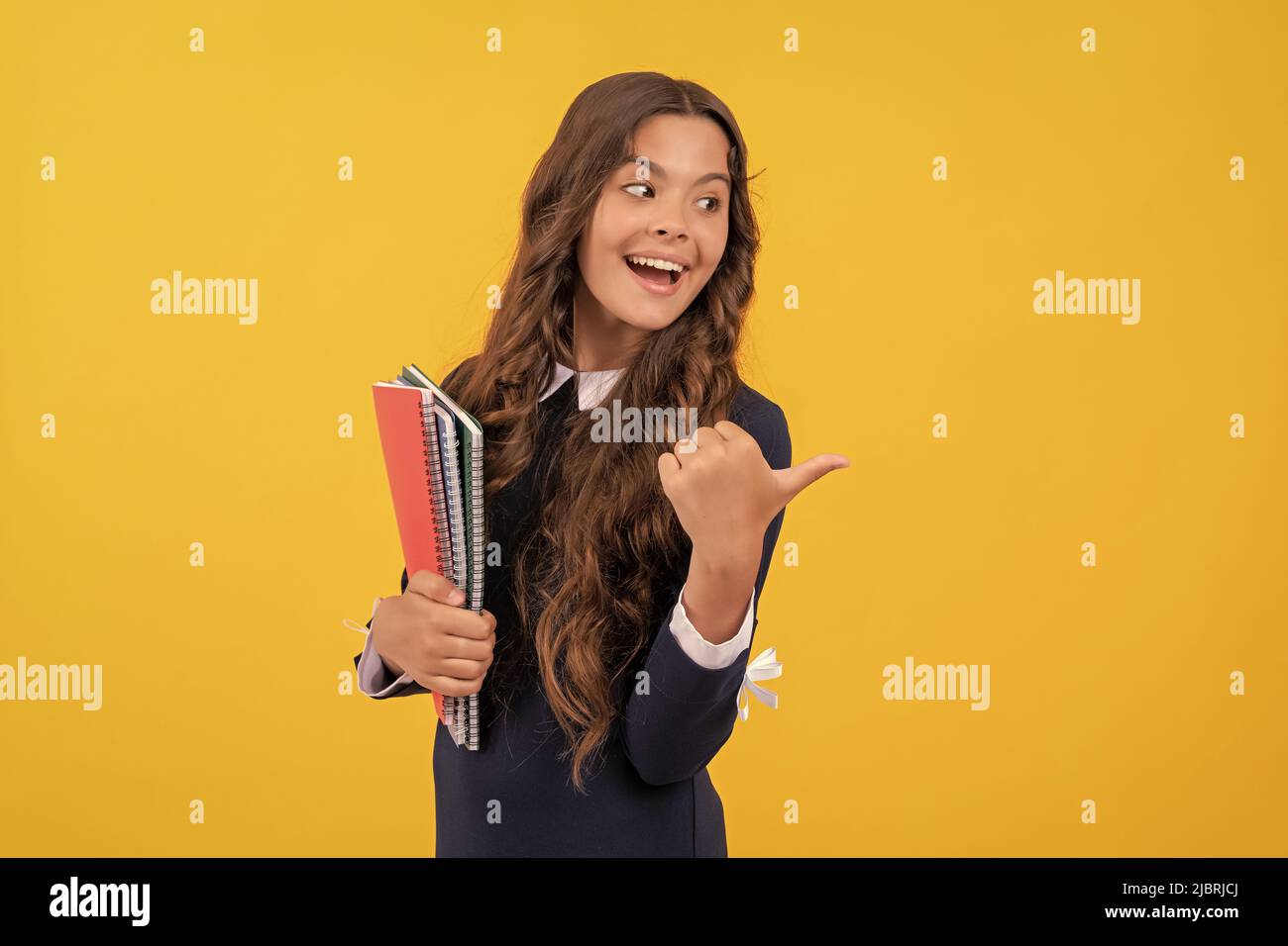 happy teen girl directing with thumb up hold school copybooks on yellow ...