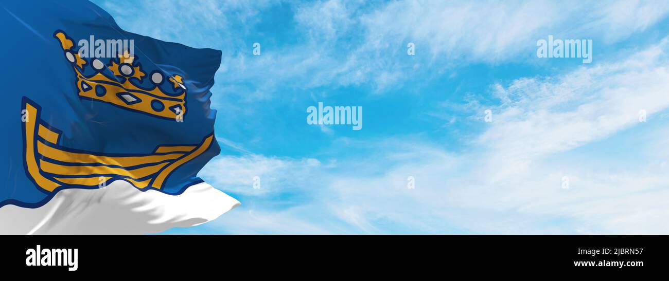 official flag of Helsinki , Finland at cloudy sky background on sunset ...