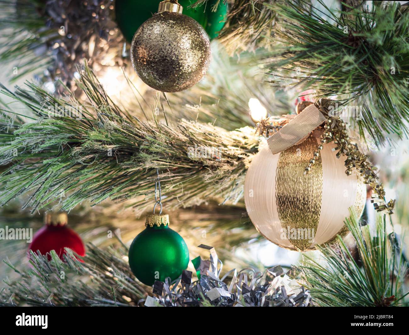 Red, green, and gold Christmas balls hanging in an evergreen tree with ...