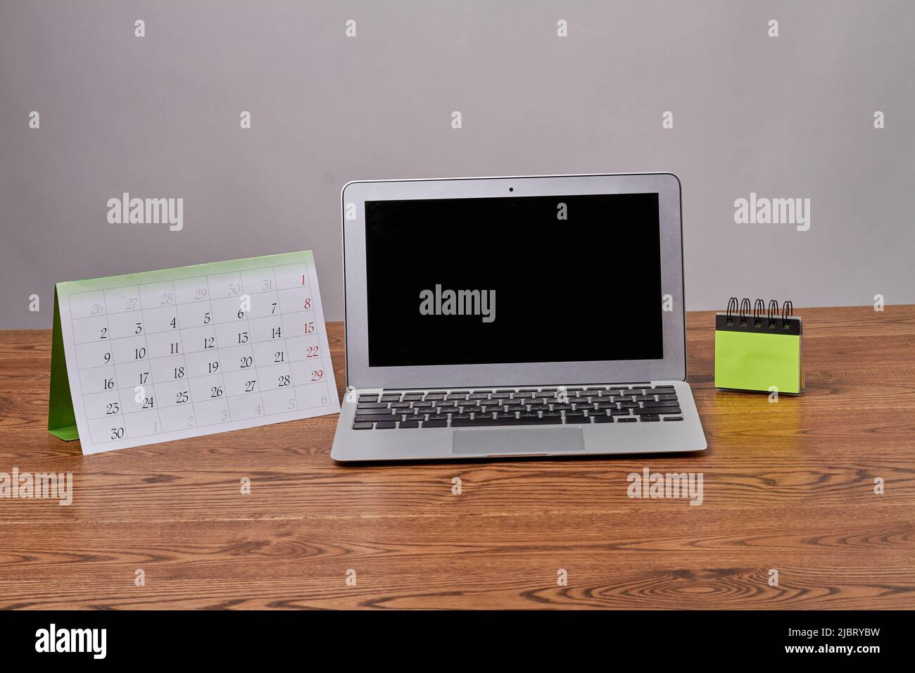 Open laptop with black screen and calendar on wooden desk. Notepad with ...