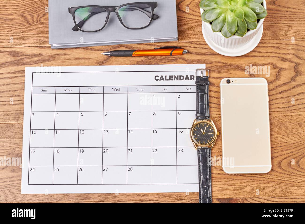 Flat lay calendar with watch clock and smartphone. Brown wooden desk ...
