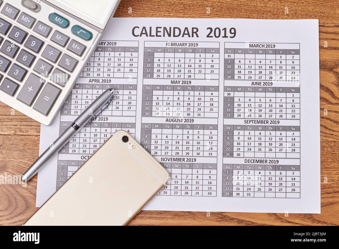 Flat lay calculator with phone and pen on the calendar. Brown wooden ...
