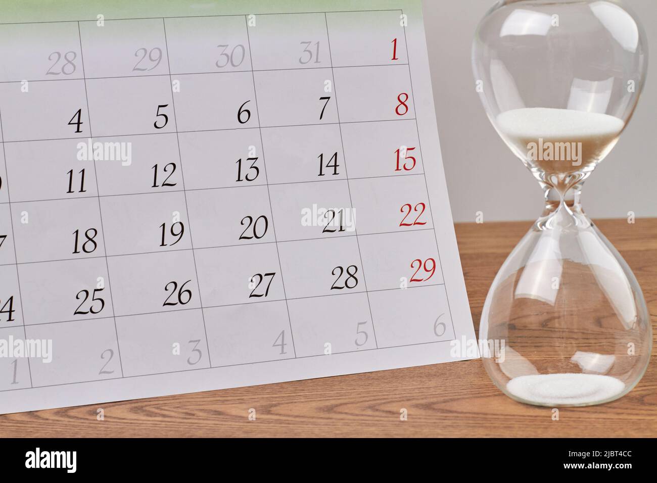 Close-up hourglass and month calendar on wooden desk. Sandglass ...