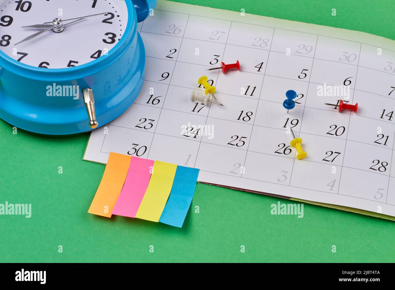 Close-up calendar with push pins and blue alarm clock. Isolated on ...