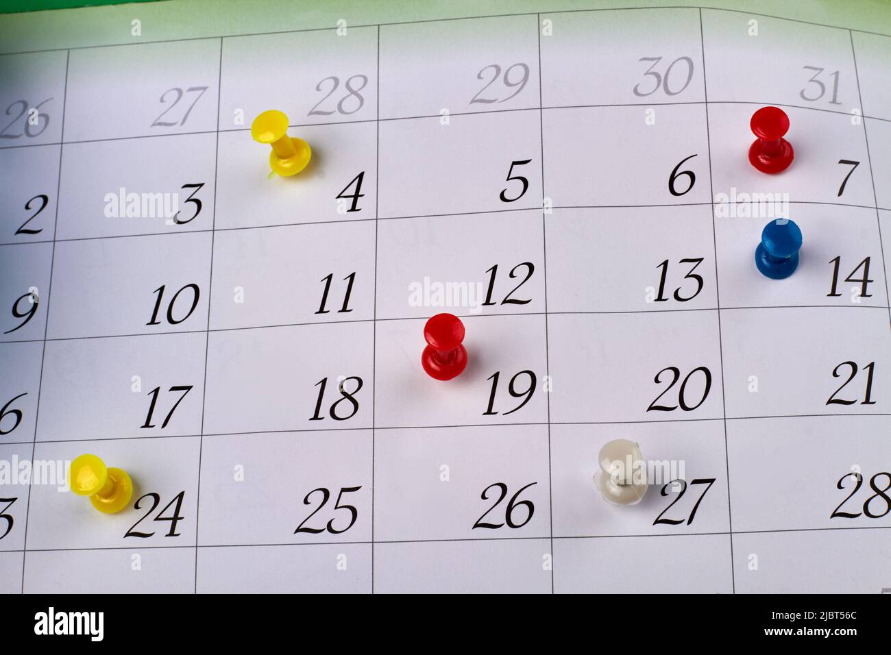 Many colorful push pins on a monthly paper calendar page. Deadlines and ...