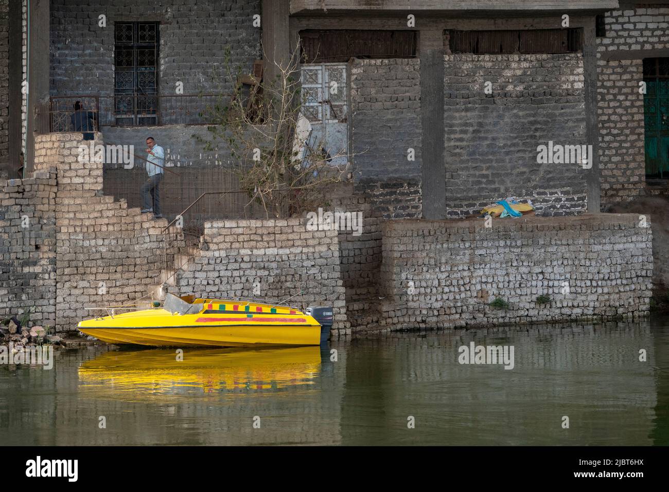 Bright yellow speed boat moored by a building block wall and half built ...