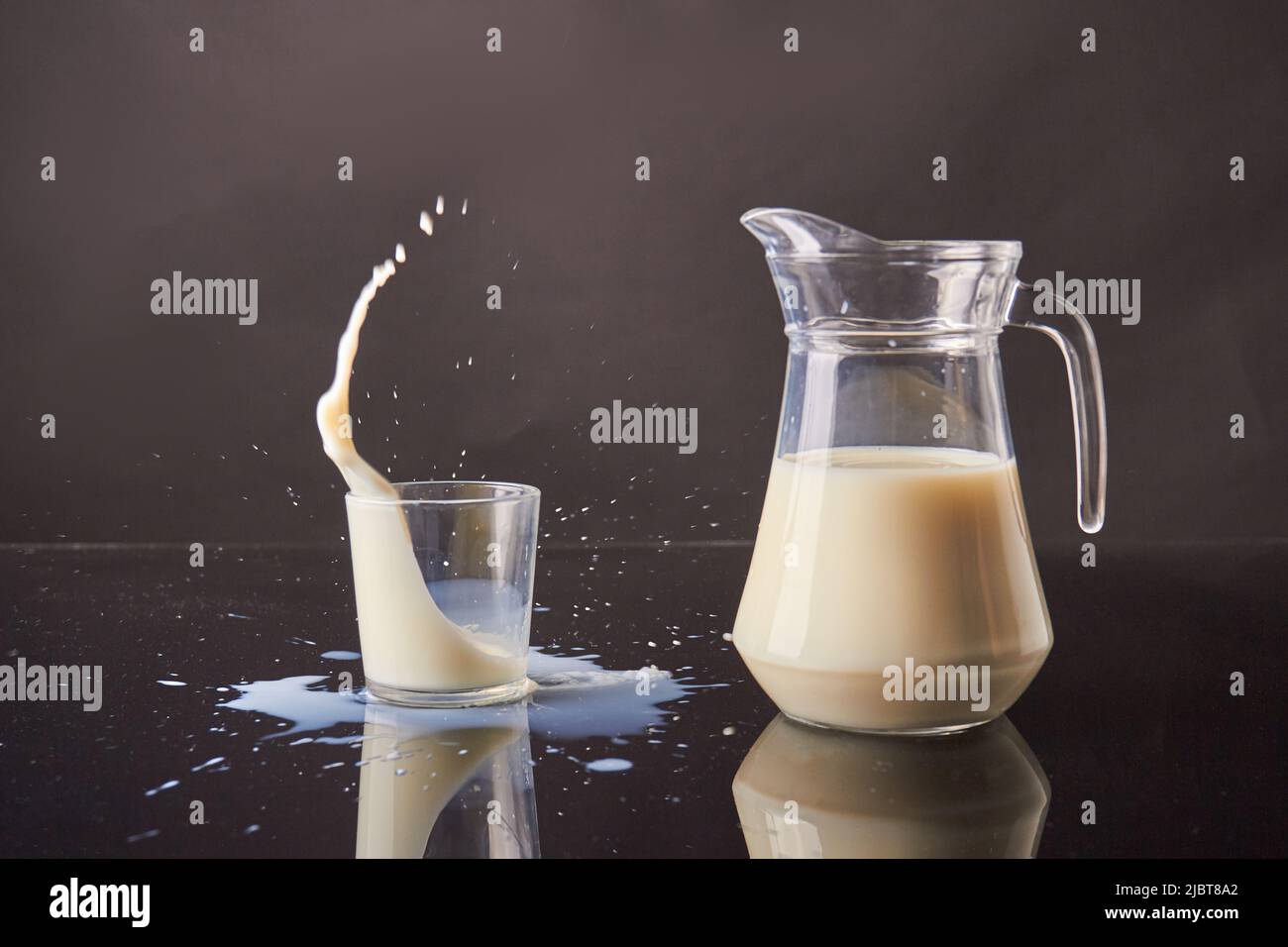 Pouring milk into glass cup and messy splashes on the reflective ...