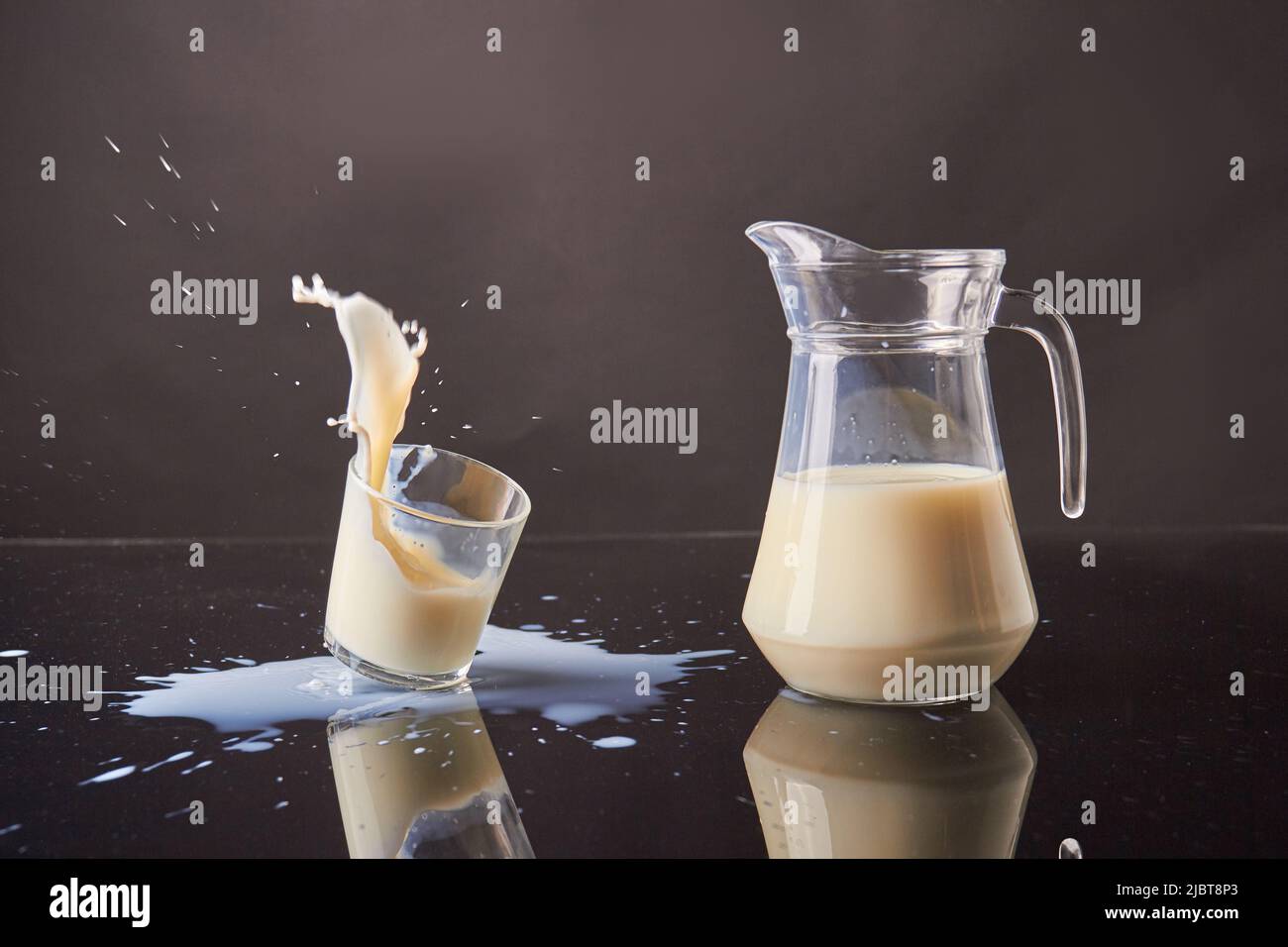 Spilling glass milk in motion and glass jug on reflective desk. Messy ...