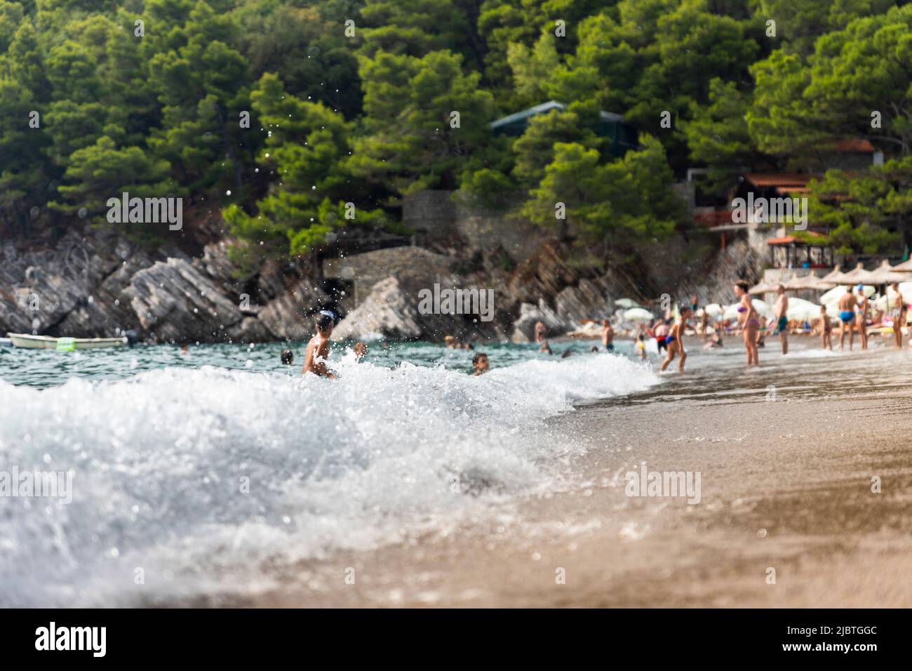 Sandy beach with spalshing waves and people swimming and enjoying ...