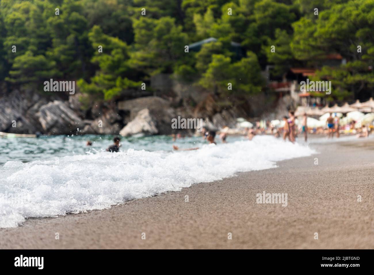 Sandy beach with spalshing waves and people swimming and enjoying ...