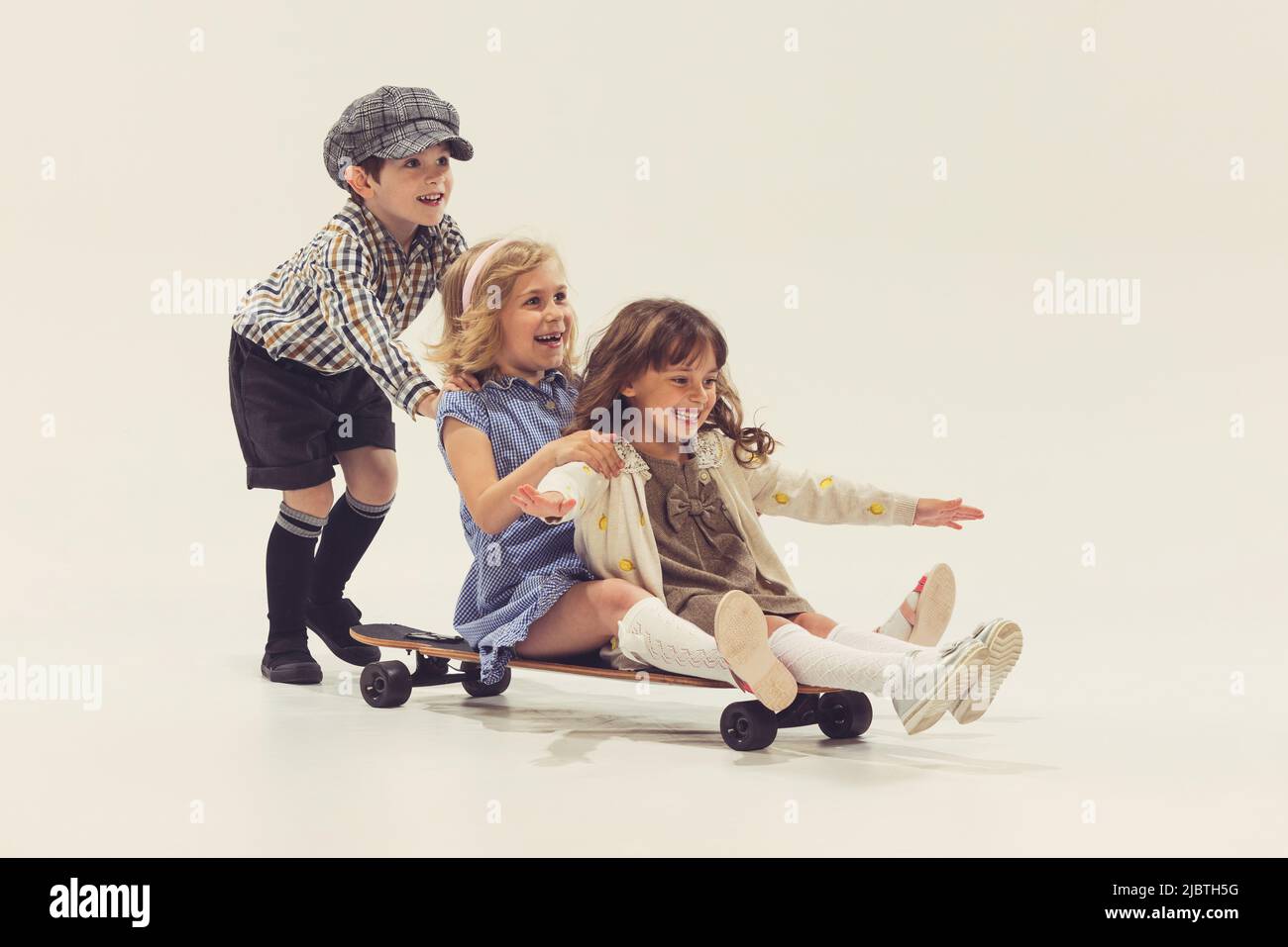 Portrait of three cheerful children playing together, boy rolling girls ...