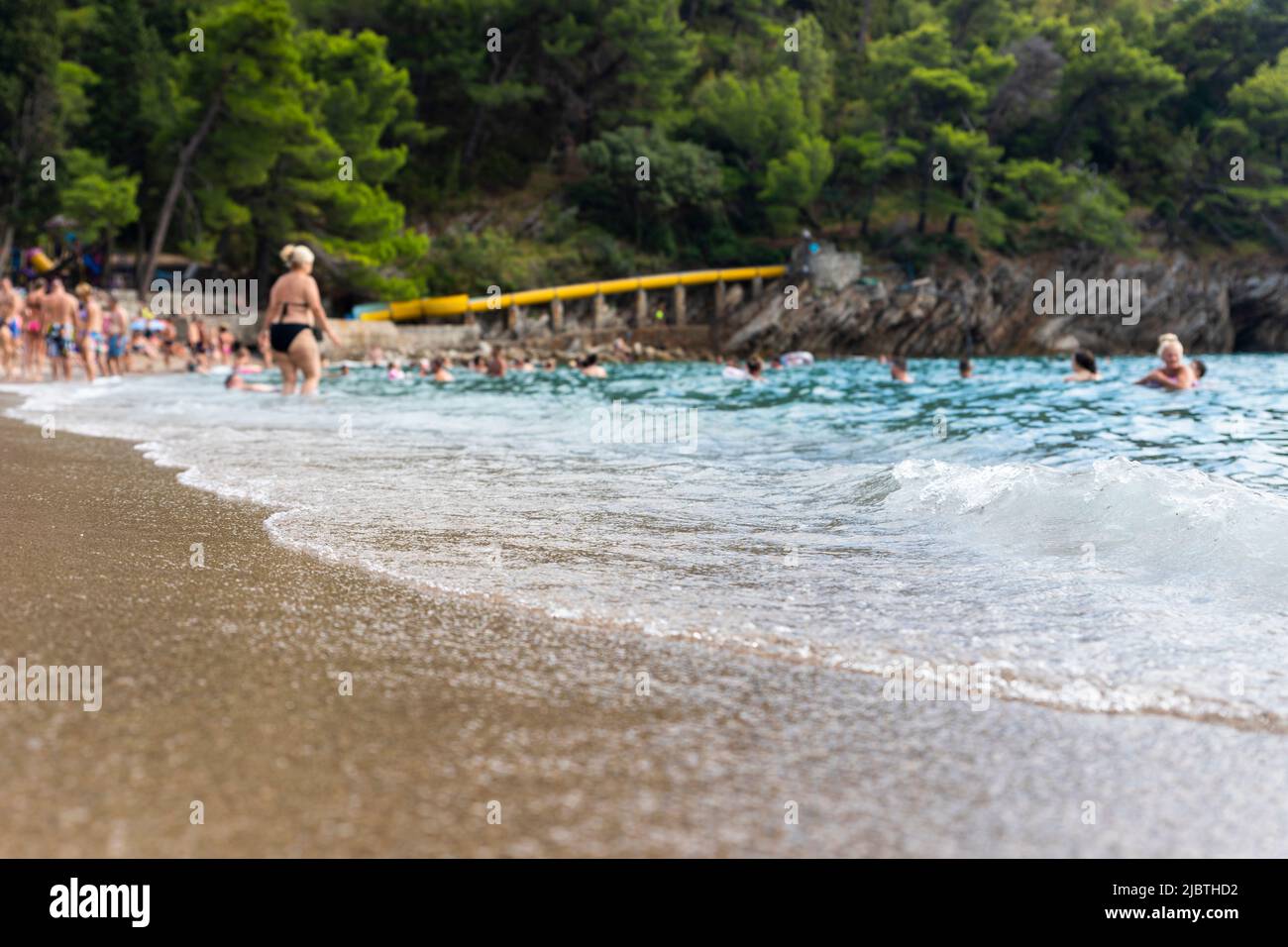 Sandy beach with spalshing waves and people swimming and enjoying ...
