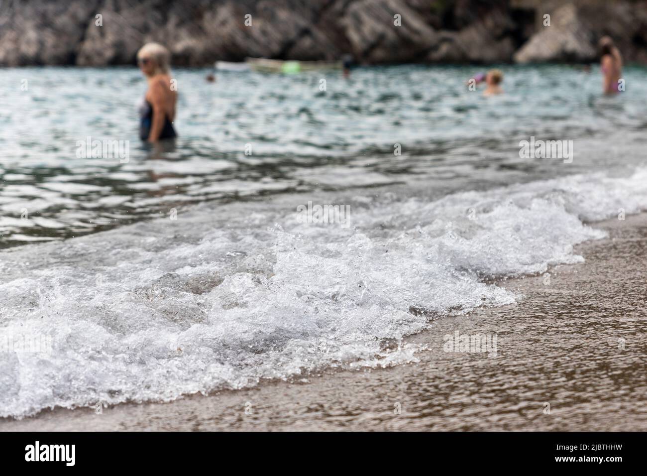 Sandy beach with spalshing waves and people swimming and enjoying ...