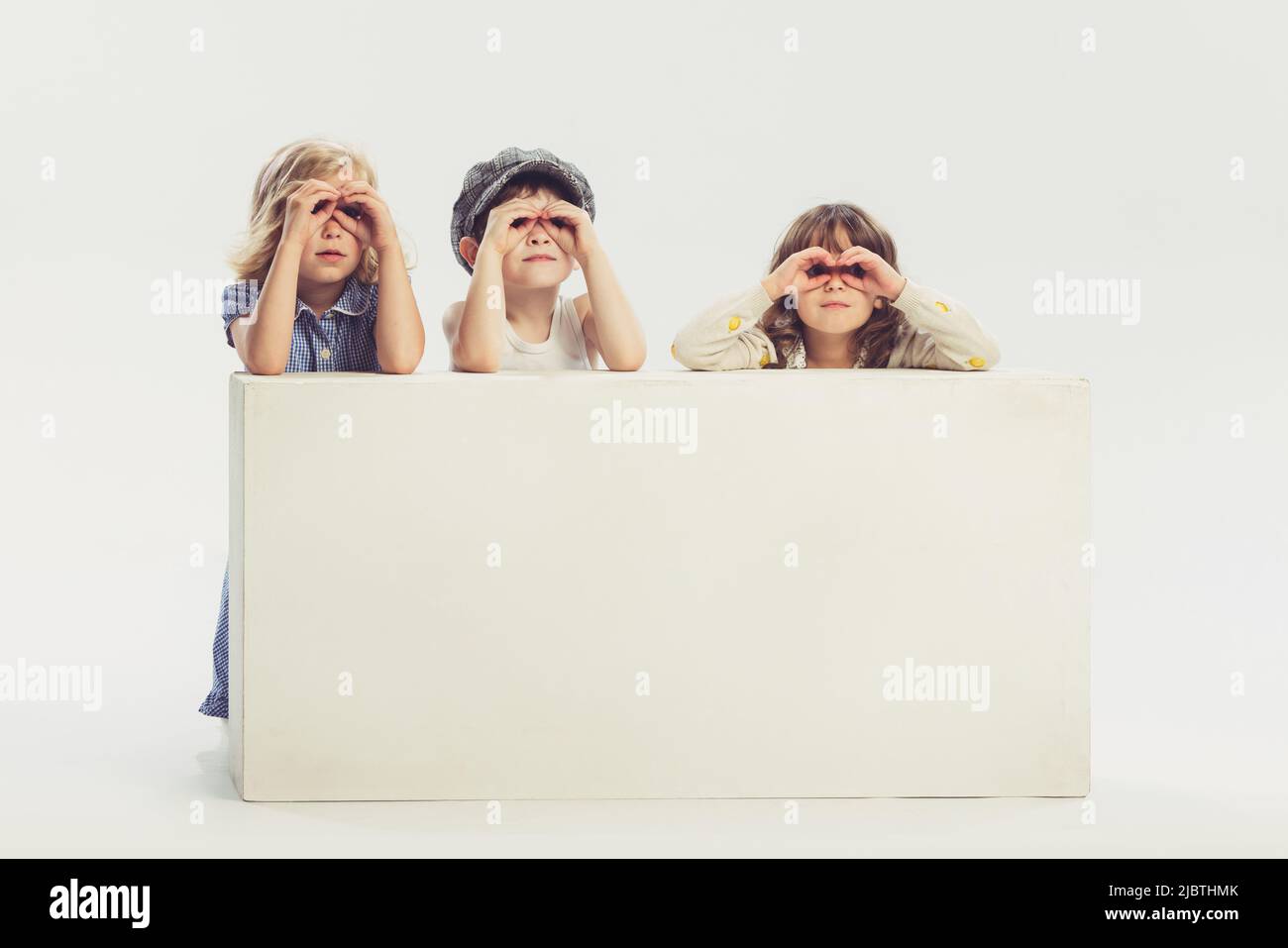 Portrait of little children, boy and two girls peeking out the table ...